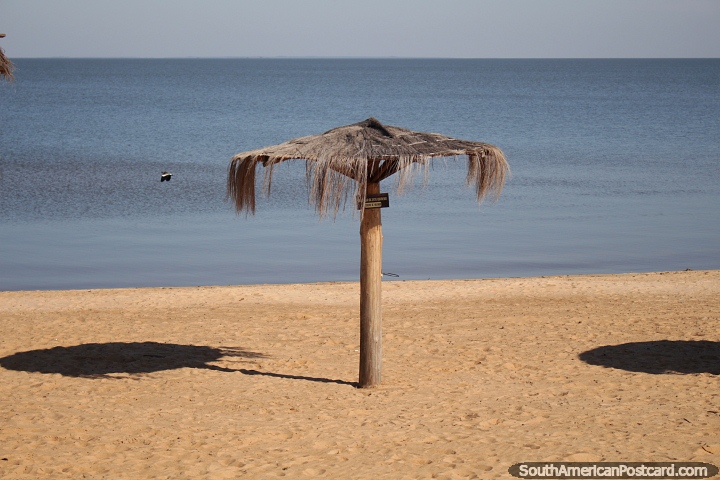 Sand, thatched umbrella and river at Tacuary Beach in Carmen del Parana ...